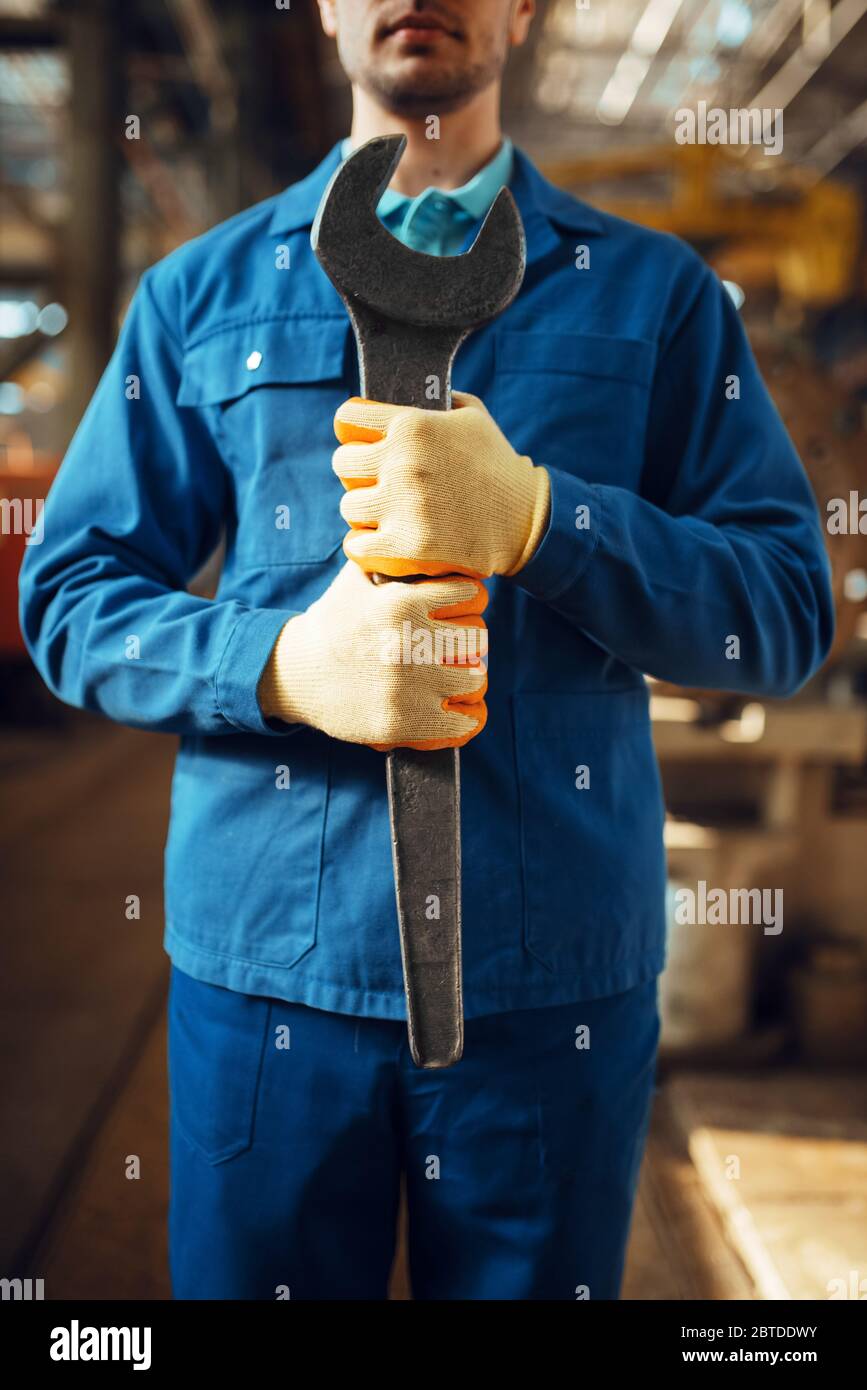Worker in uniform holds large wrench on factory Stock Photo - Alamy