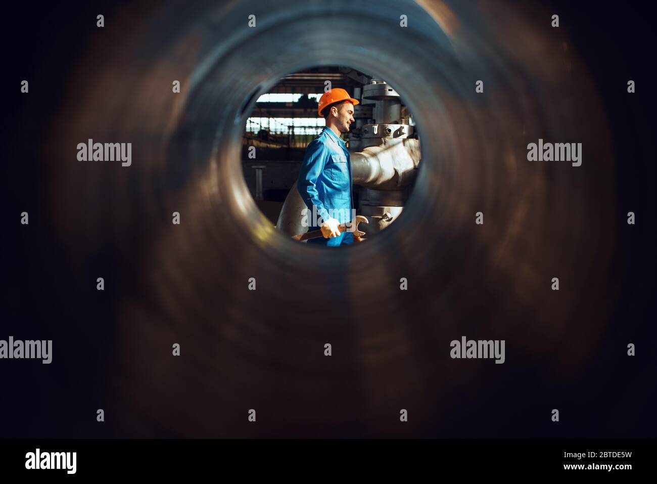 Worker with wrench on factory, view through tube Stock Photo - Alamy