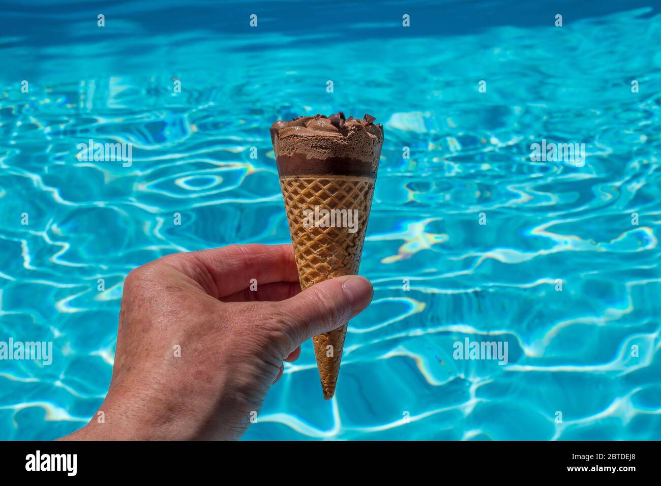 Eating Chocolate ice cream cone with sunlit blue swimming pool water in ...