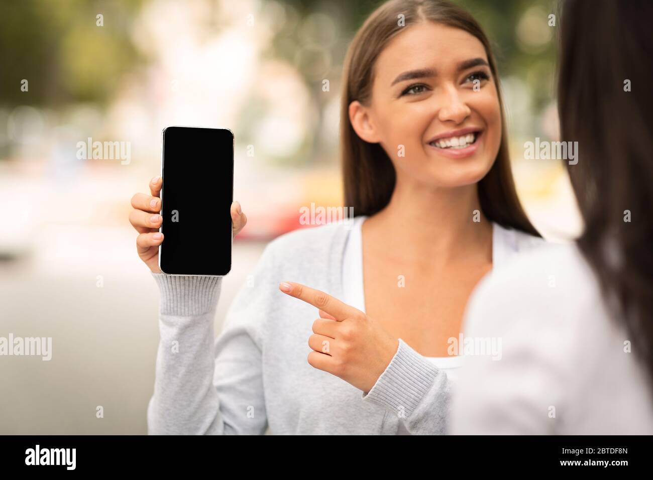 Girl Showing Smartphone Blank Screen To A Friend Walking Outside Stock ...