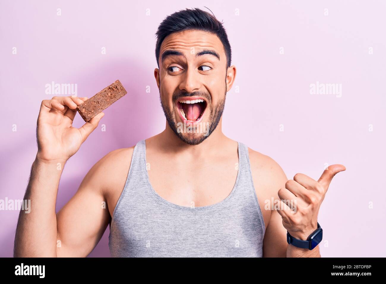Young handsome man with beard eating energy protein bar over isolated ...