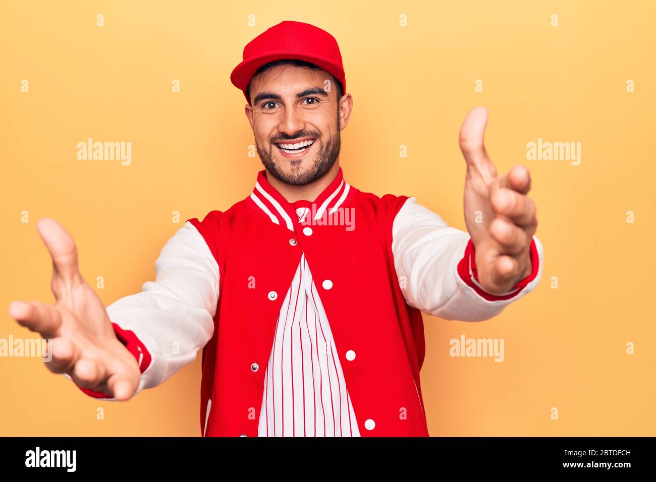 Handsome sporty man with beard wearing baseball jacket and cap over ...