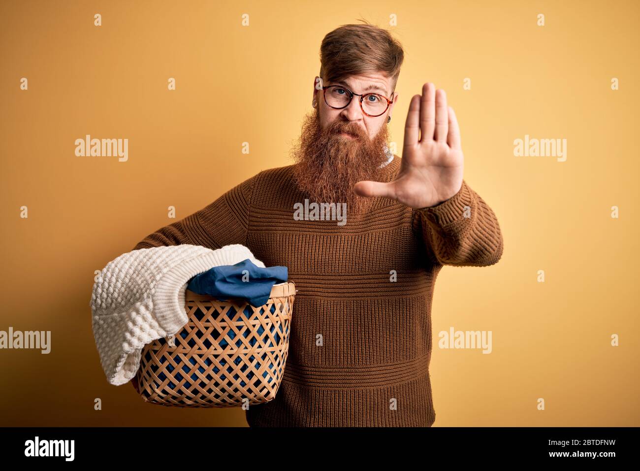 Redhead Irish Man With Beard Doing Housework Laundry Over Yellow Background With Open Hand Doing