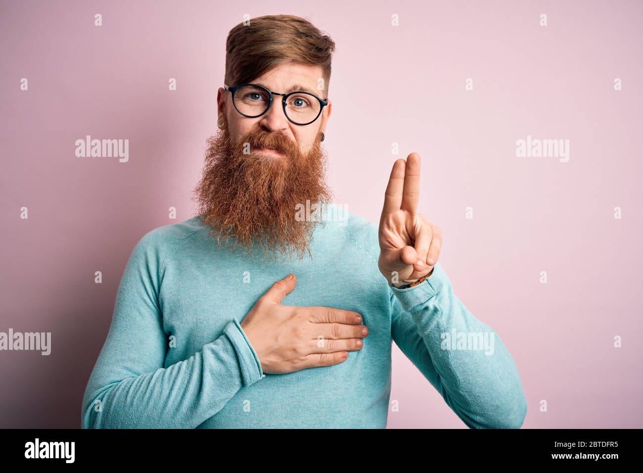 Handsome Irish redhead man with beard wearing glasses over pink ...
