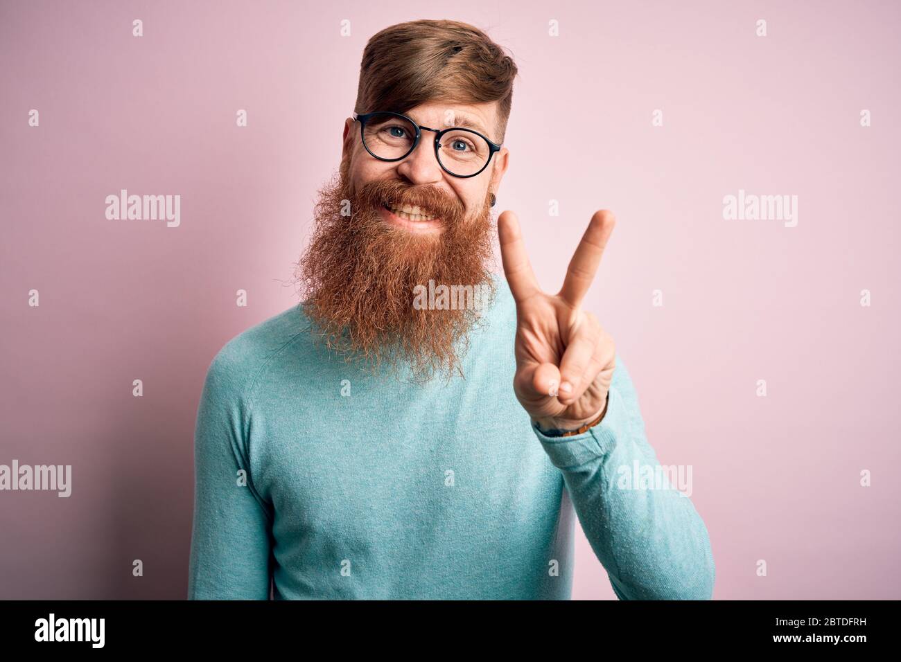 Handsome Irish redhead man with beard wearing glasses over pink ...
