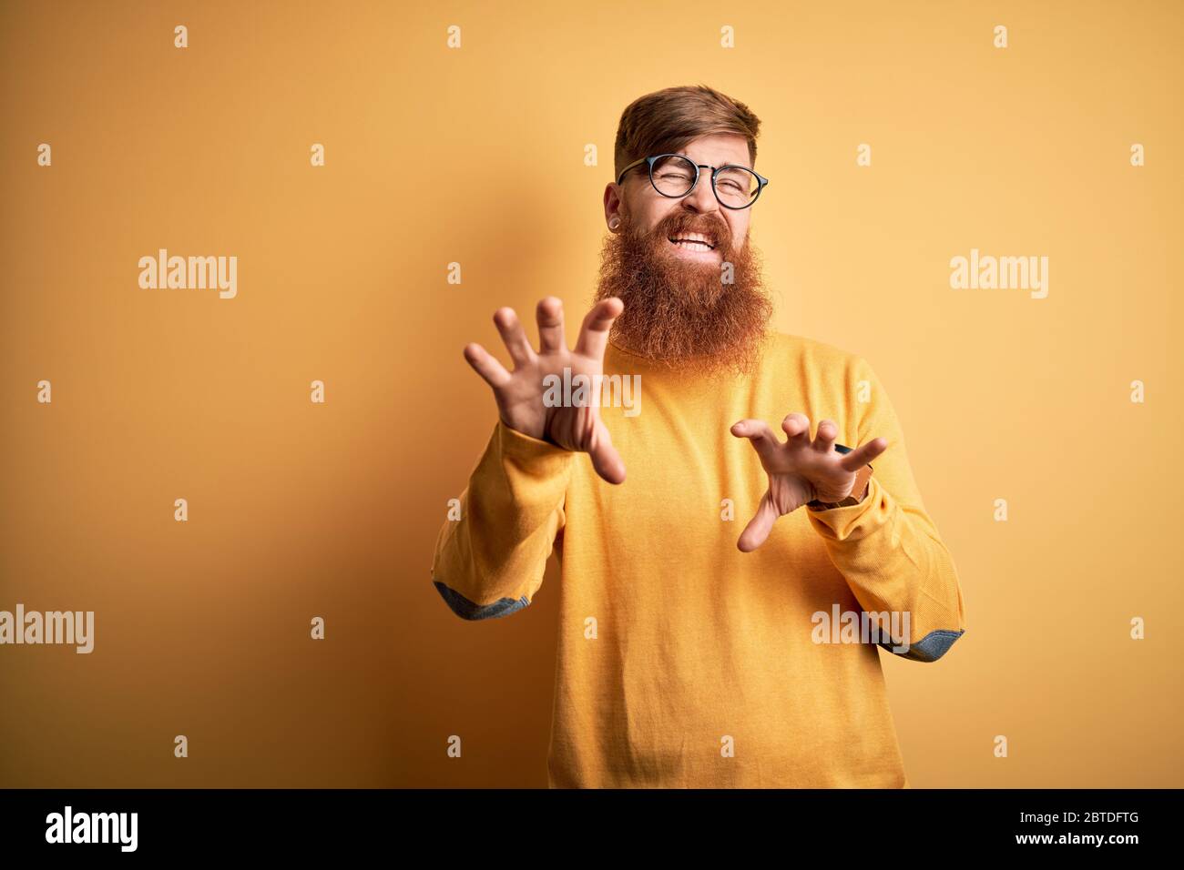 Handsome Irish redhead man with beard wearing glasses over yellow ...