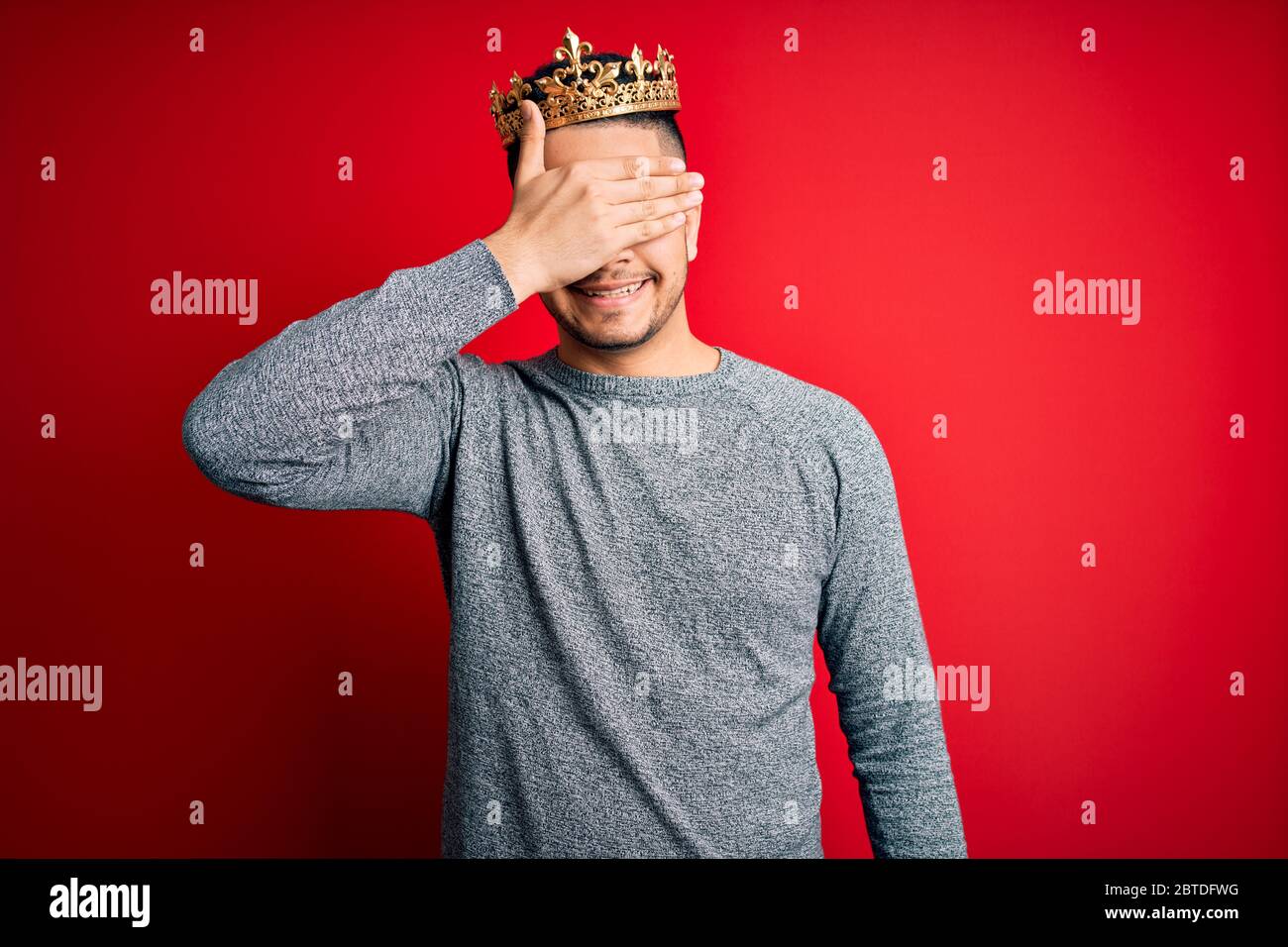 Young handsome man wearing golden crown of prince over isolated red ...