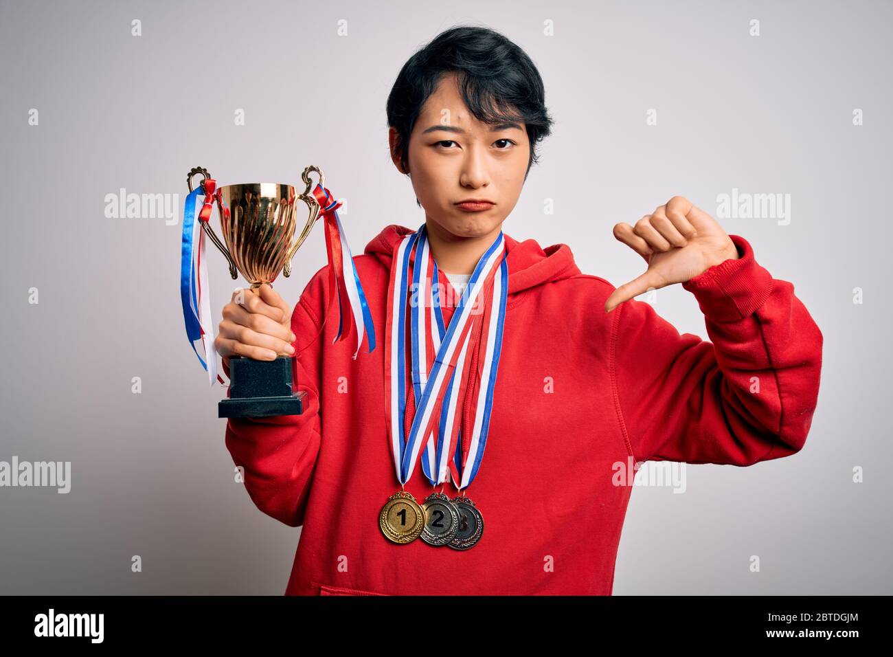Young beautiful asian girl winner holding trophy wearing medals over ...