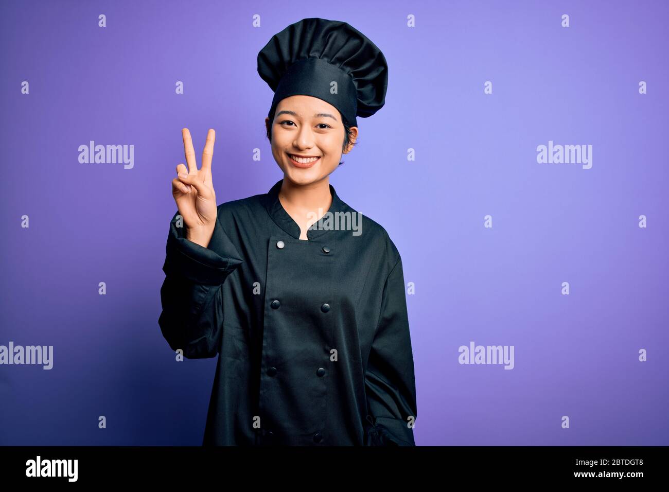 Young beautiful chinese chef woman wearing cooker uniform and hat over ...