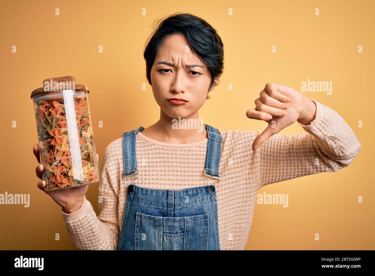Young beautiful asian girl holding jar with italian dry pasta over ...