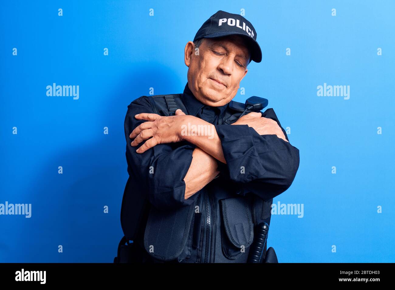 Senior man with grey hair wearing police uniform hugging oneself happy ...