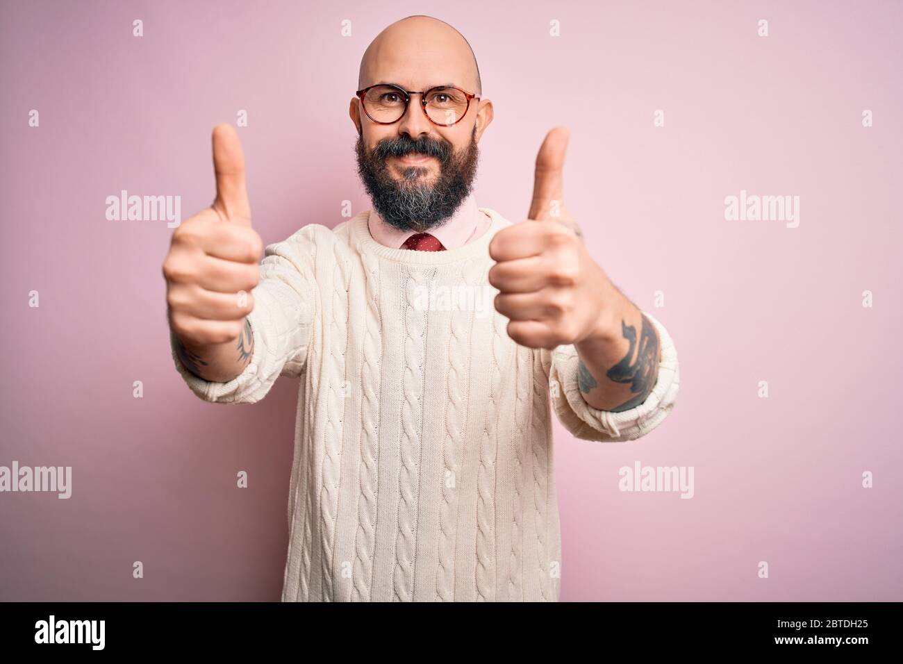 Handsome bald man with beard and tattoo wearing glasses and sweater ...