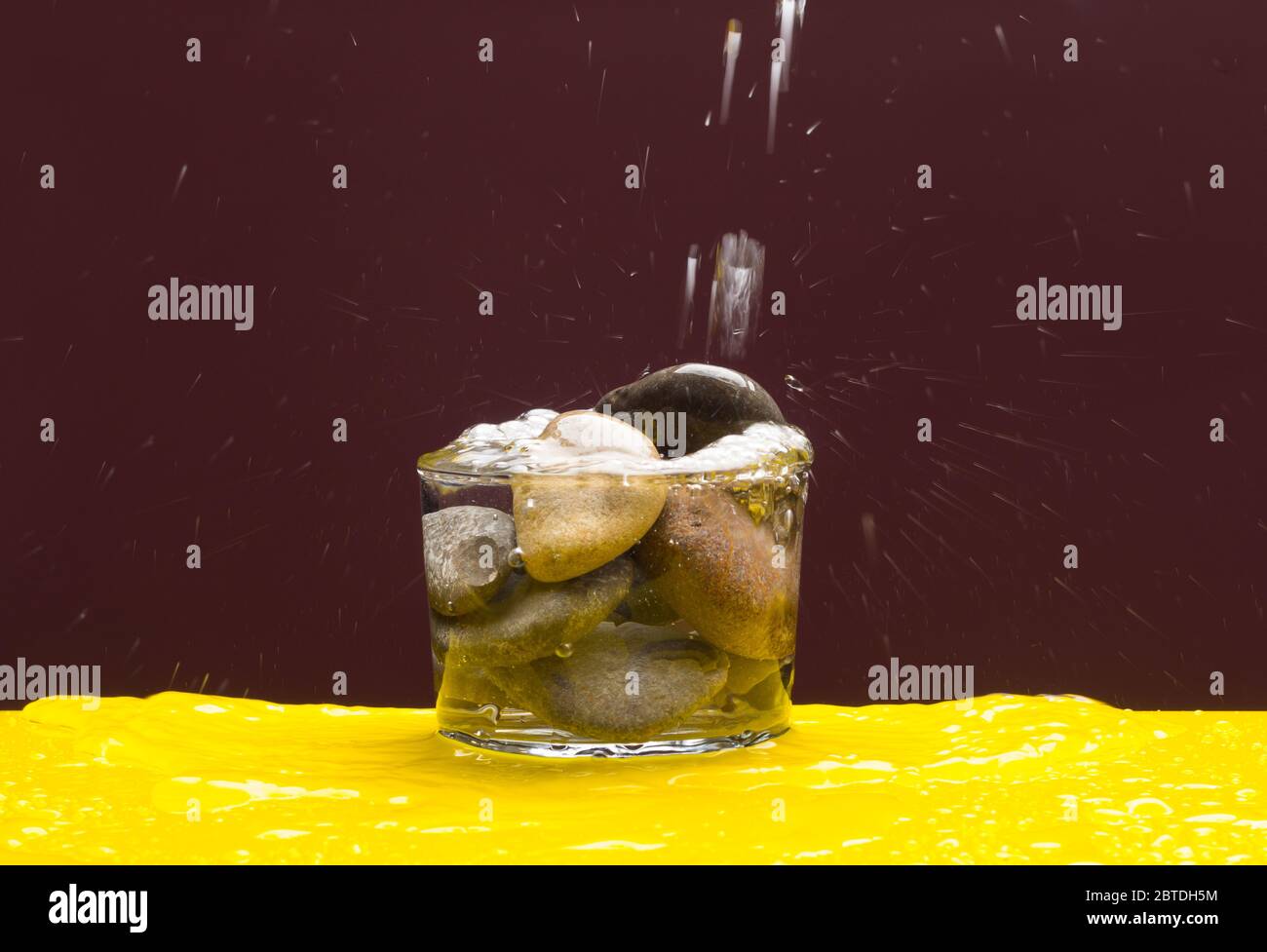 Transparent glass cup with stones inside and water splashing and ...