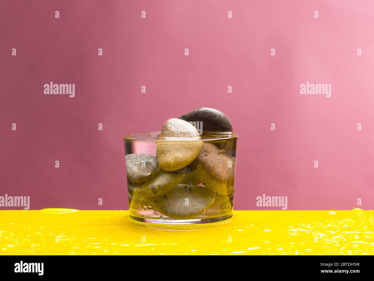 Transparent glass cup with stones inside and water splashing and ...