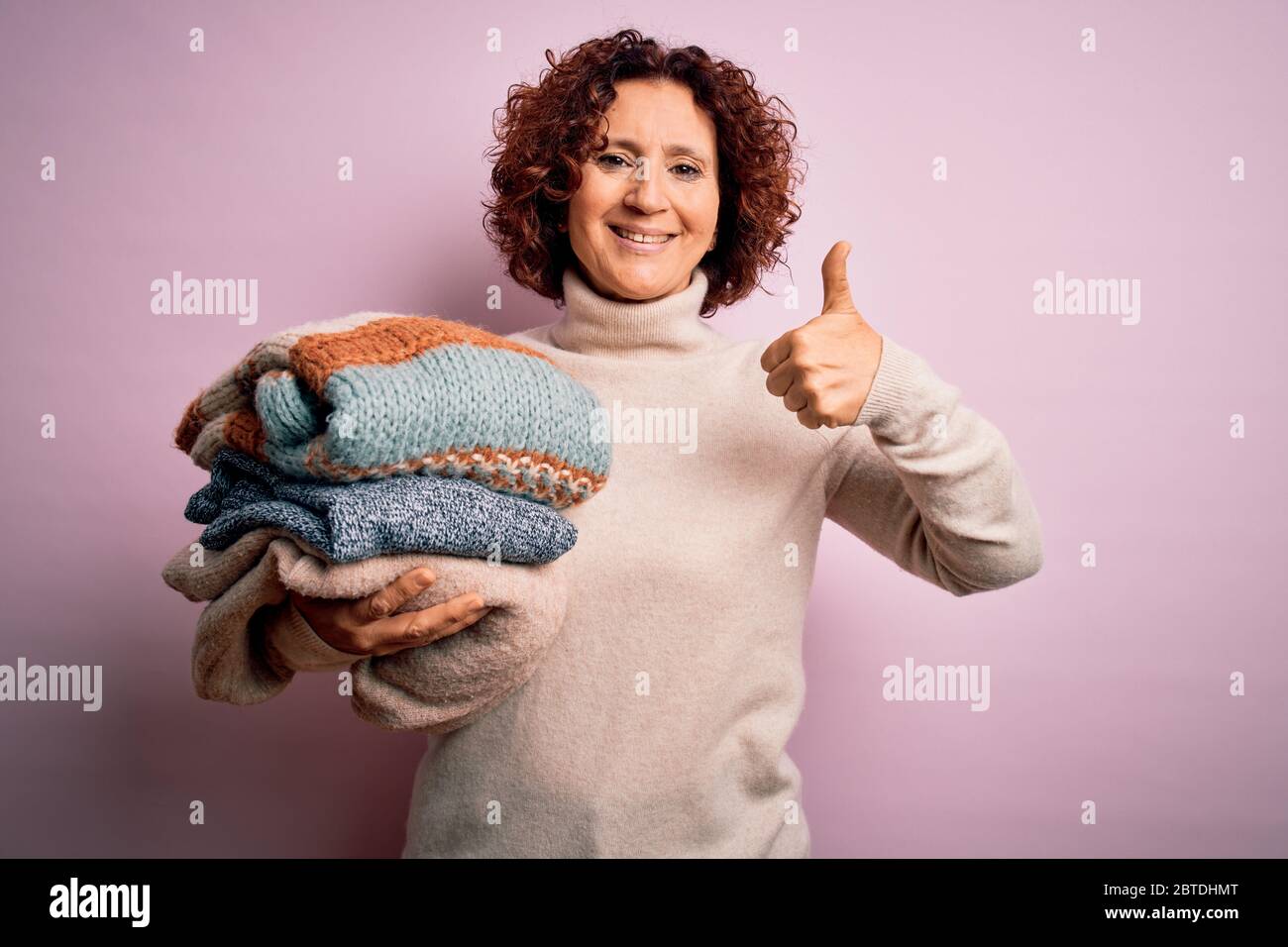 Middle age curly hair housework woman holding pile of clothes over ...