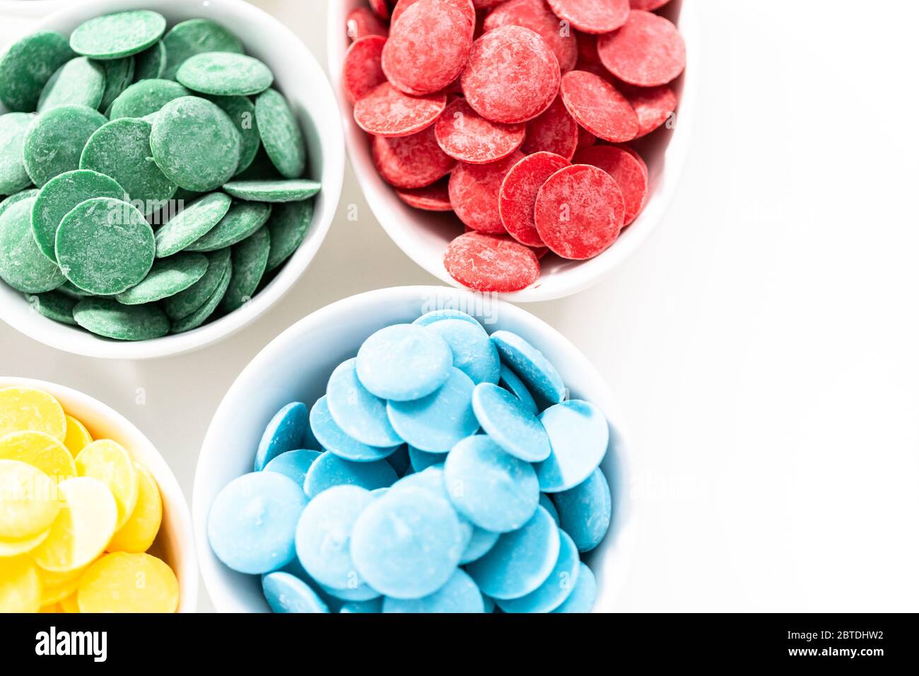 Rainbow colors of round chocolate chips in a white bowls for melting ...