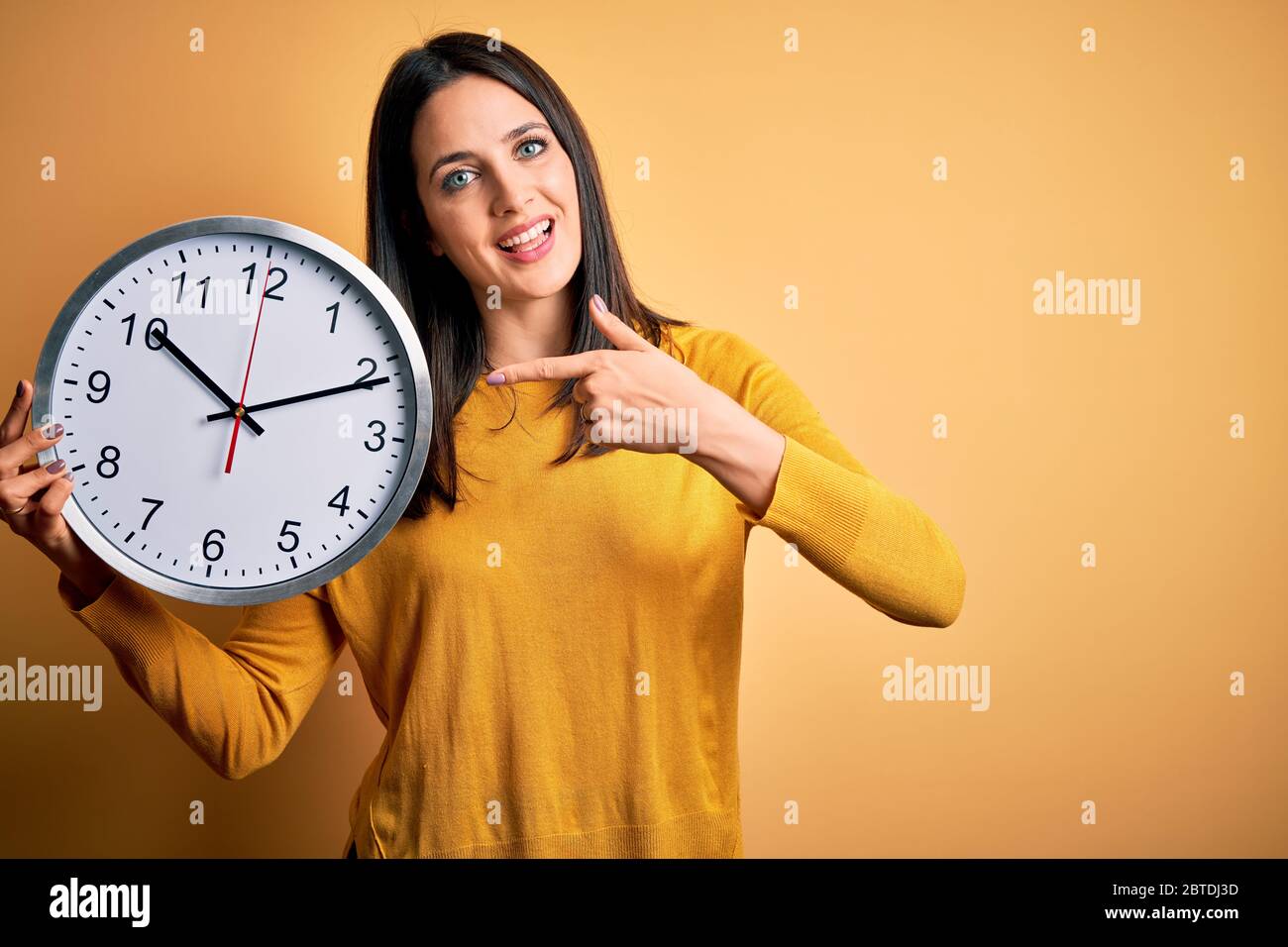 Young woman with blue eyes doing countdown holding big clock over ...