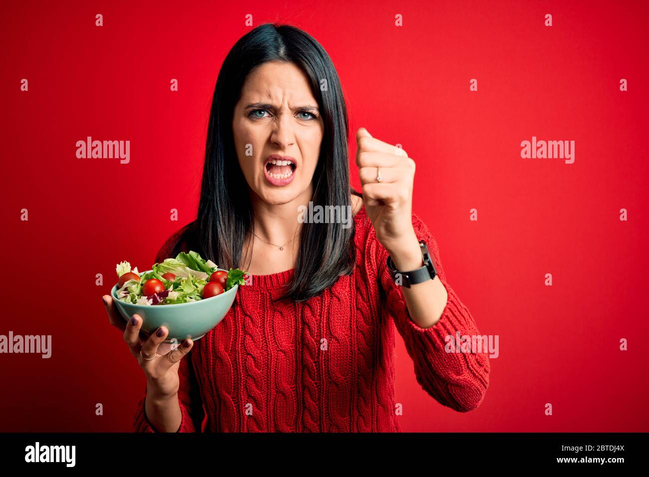 Young brunette woman with blue eyes eating healthy green salad over ...