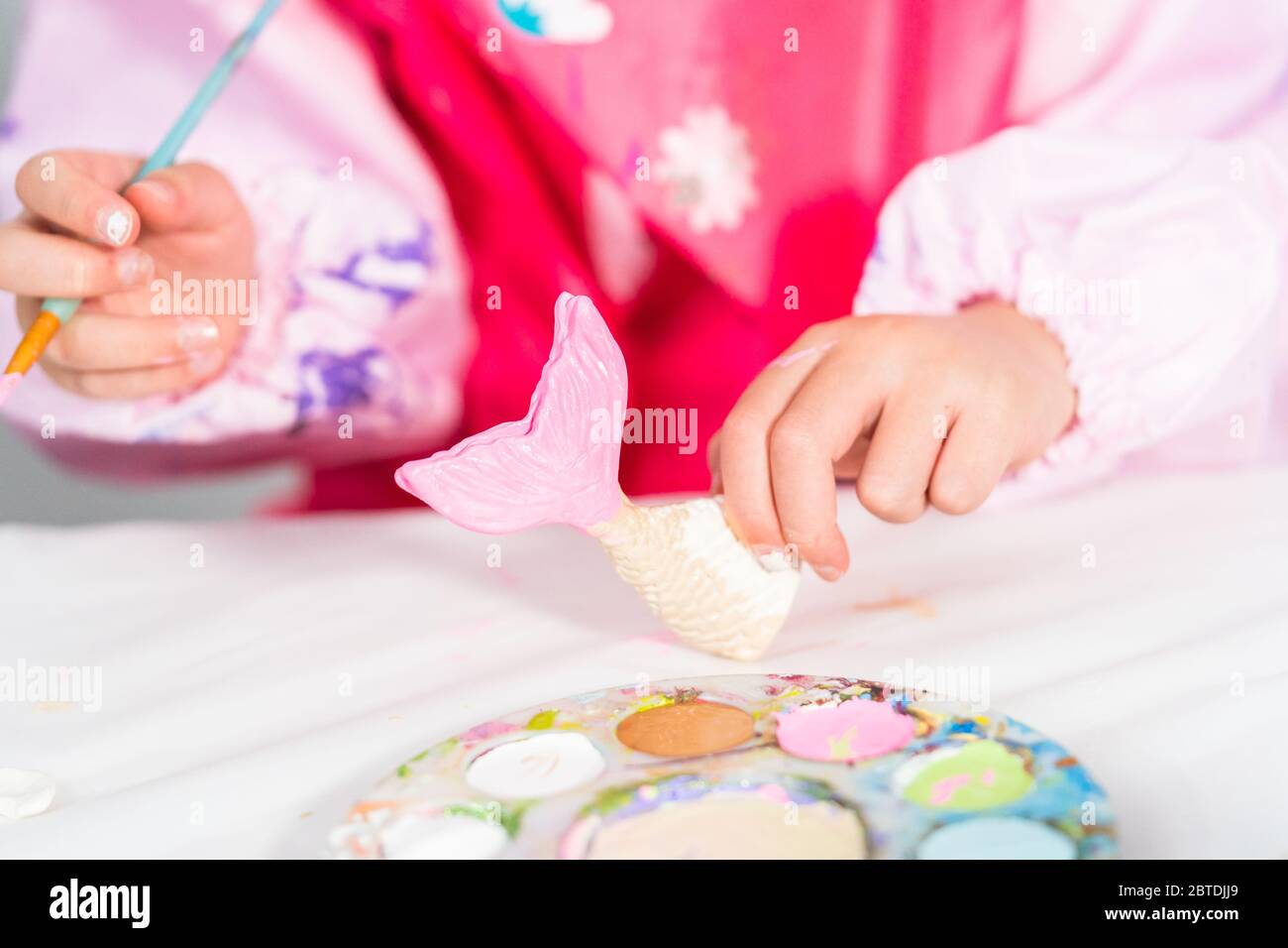 Little girl painting mermaid tails made out of modeling clay with ...