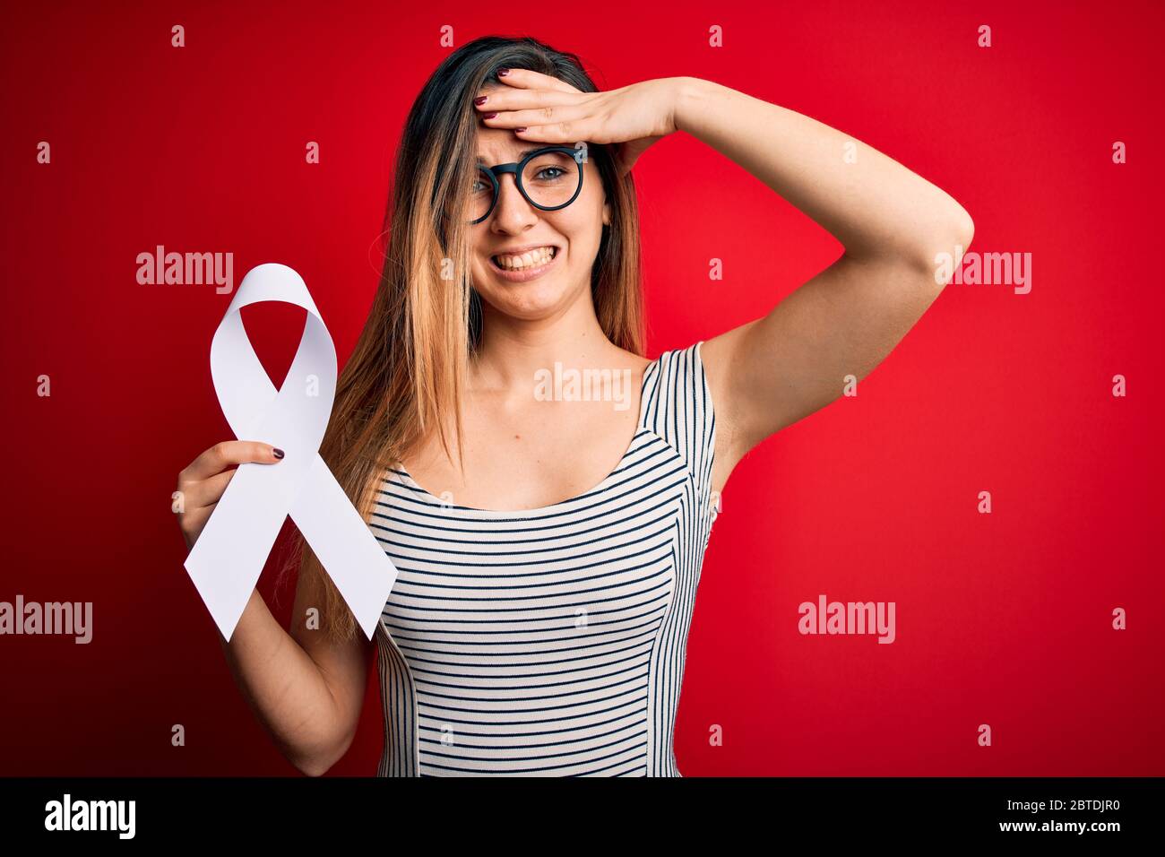 Young beautiful blonde woman with blue eyes holding white ribbon over ...