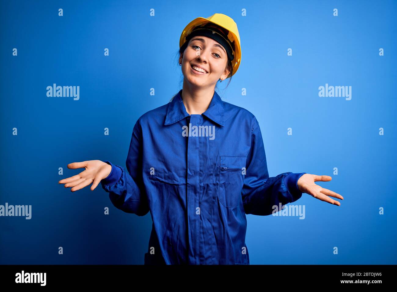 Young beautiful worker woman with blue eyes wearing security helmet and ...