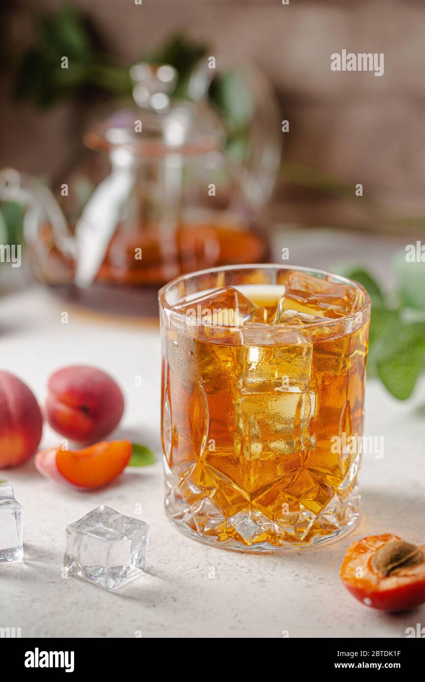 Glass of peach or apricot iced tea with fruit slices against white ...