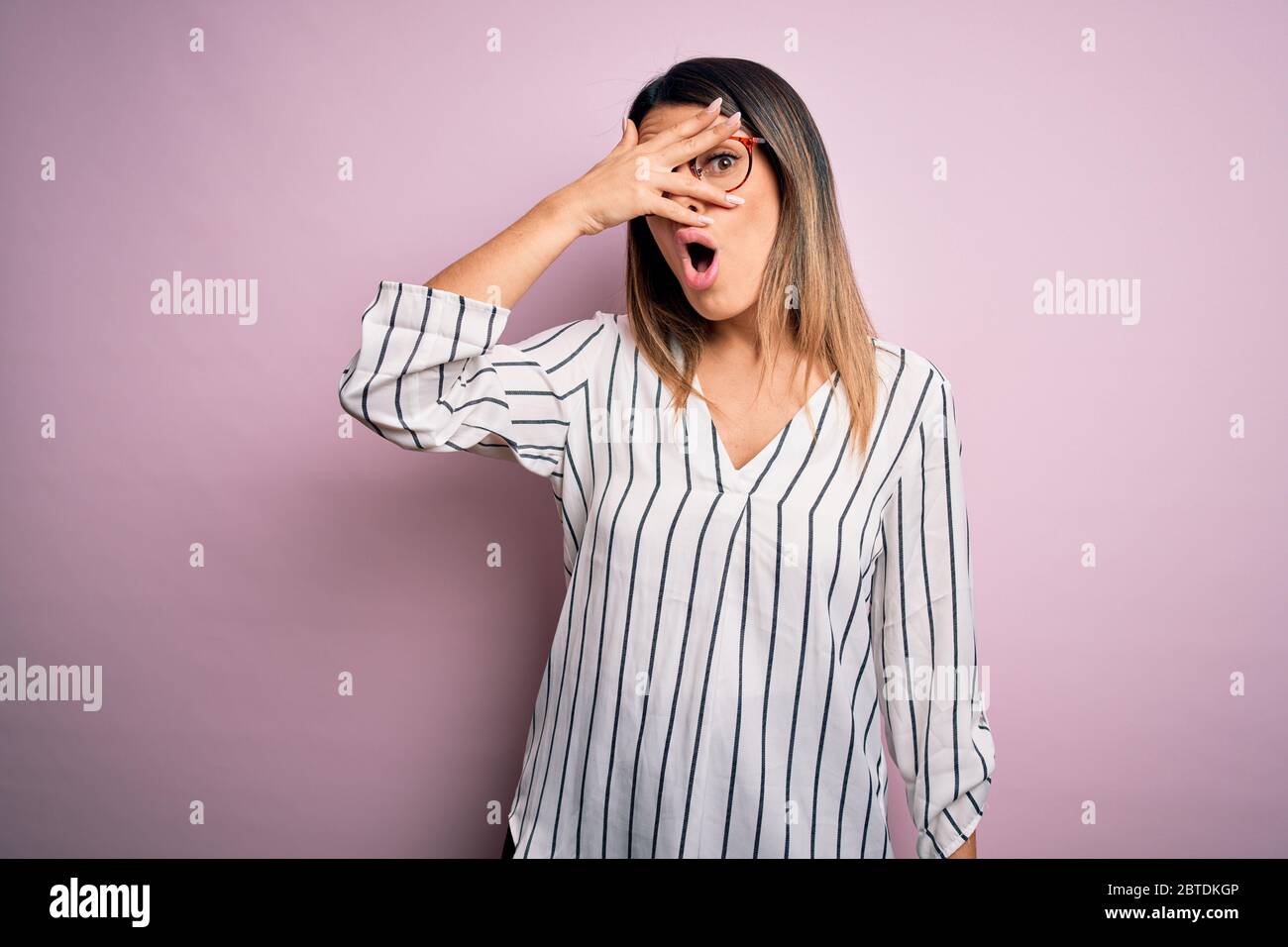 Young beautiful woman wearing casual striped t-shirt and glasses over ...