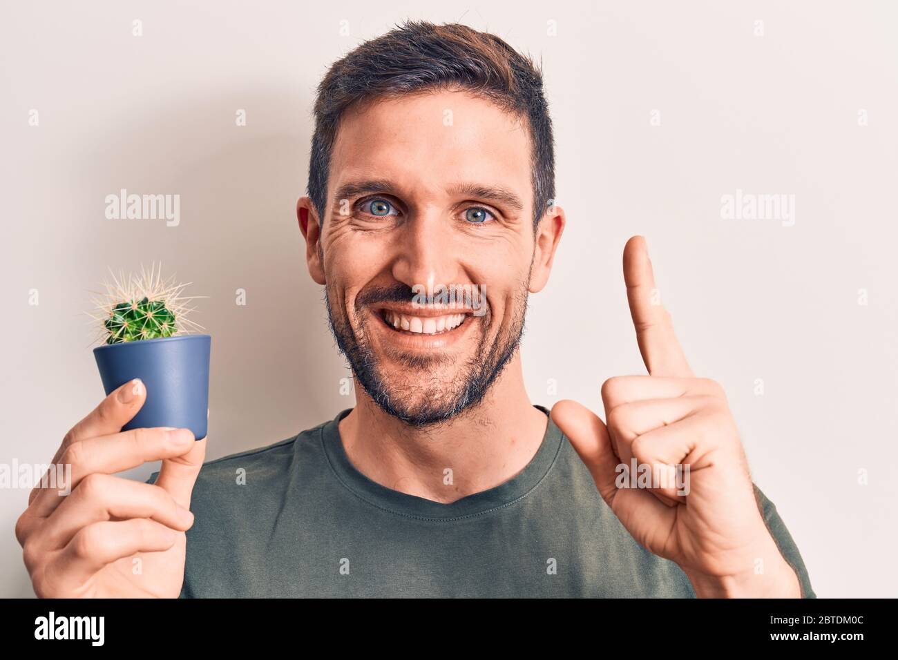 Young handsome man holding small cactus plant pot over isolated white ...