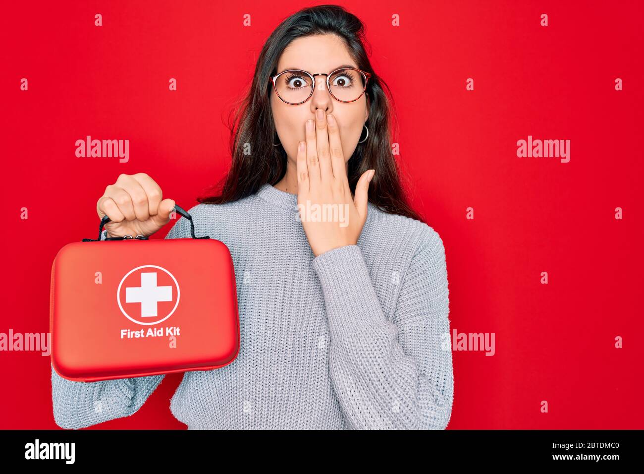 Young beautiful girl holding first aid kit medical box over red ...