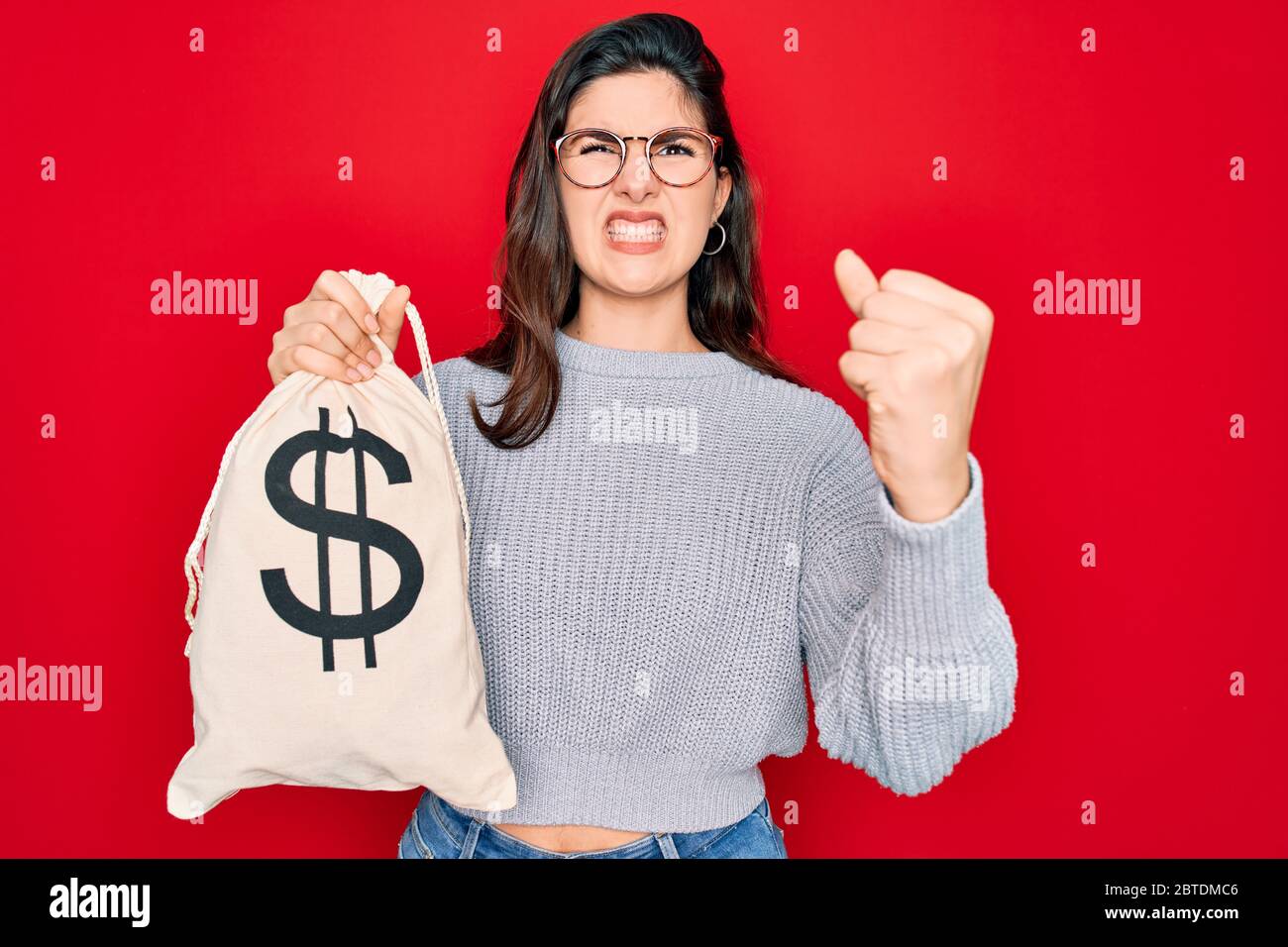 Young beautiful girl holding money bag with dollar symbol for business ...