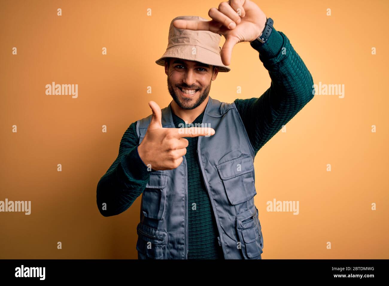 Handsome tourist man with beard on vacation wearing explorer hat over ...