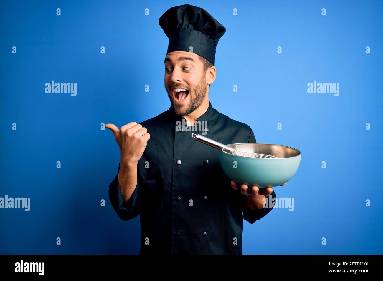 Young cooker man with beard wearing uniform using whisk and bowl over ...