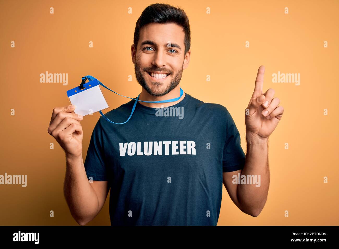Handsome volunteer man with beard holding id card identification over ...
