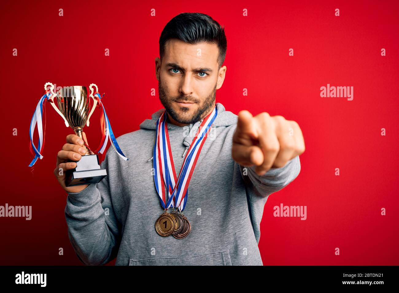 Young handsome succesful man holding trophy wearing medals over red ...