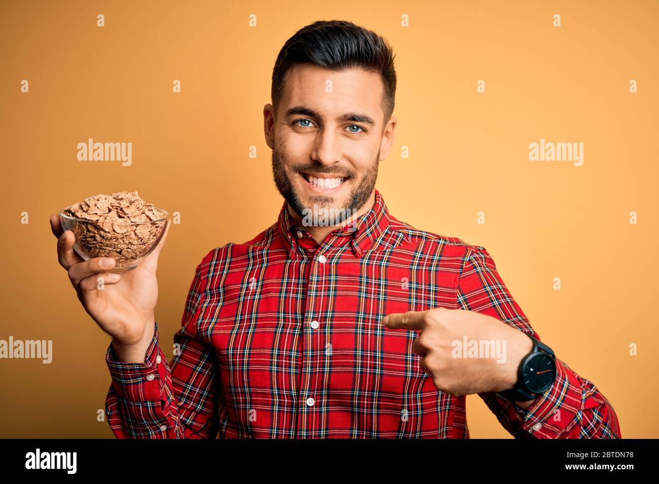 Young handsome man eating classic wholemeal cereals over yellow ...