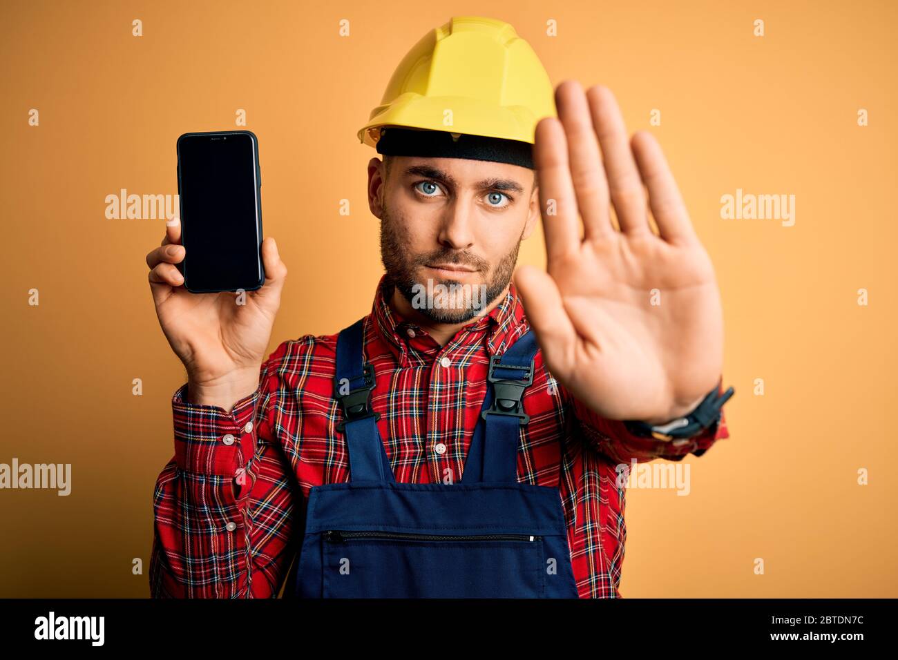 Young builder man wearing safety helmet showing smartphone screen over ...