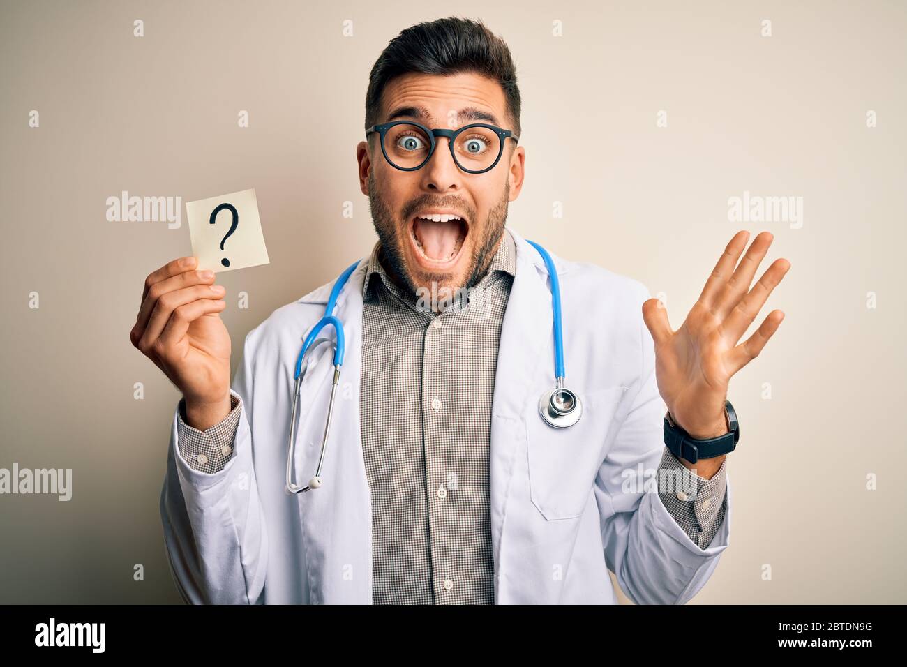 Young doctor man wearing stethoscope holding question mark reminder ...
