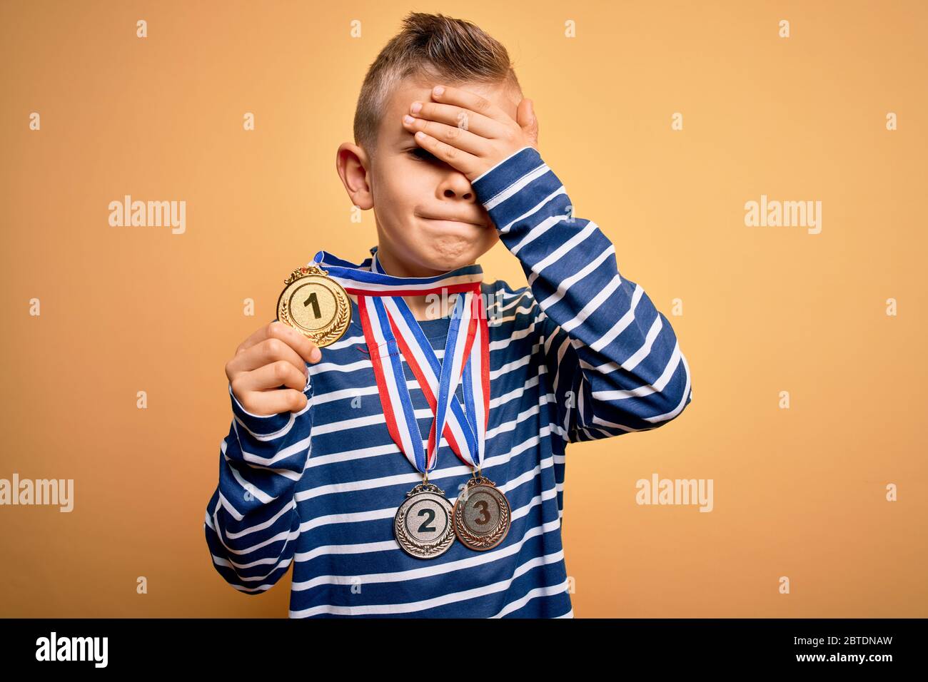 Young little caucasian winner kid wearing award competition medals over ...