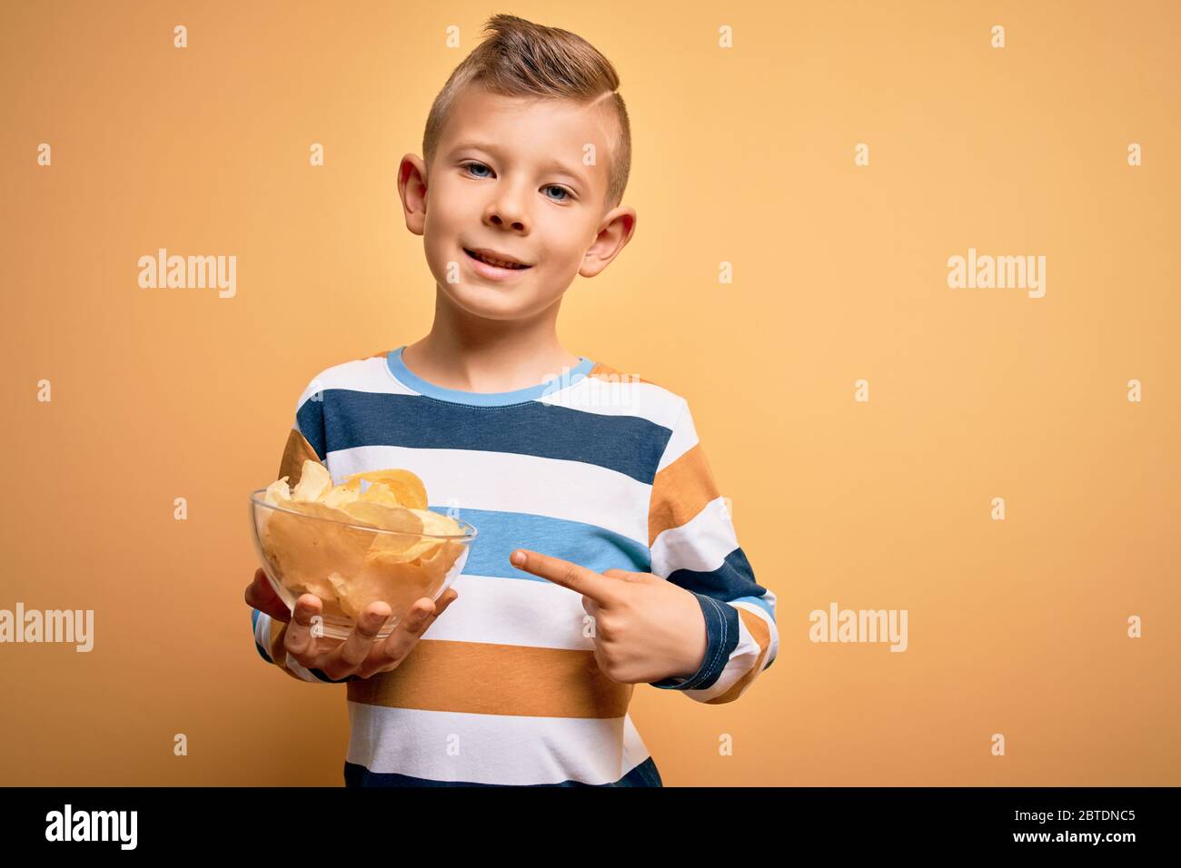 Young little caucasian kid eating unheatlhy potatoes crisps chips over ...