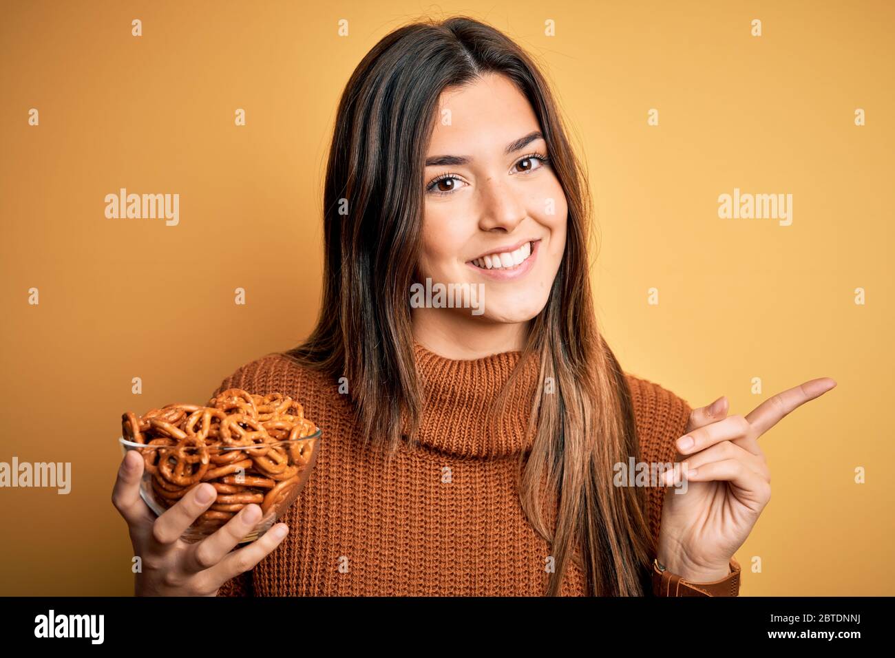 Young beautiful girl eating baked german pretzel standing over isolated ...
