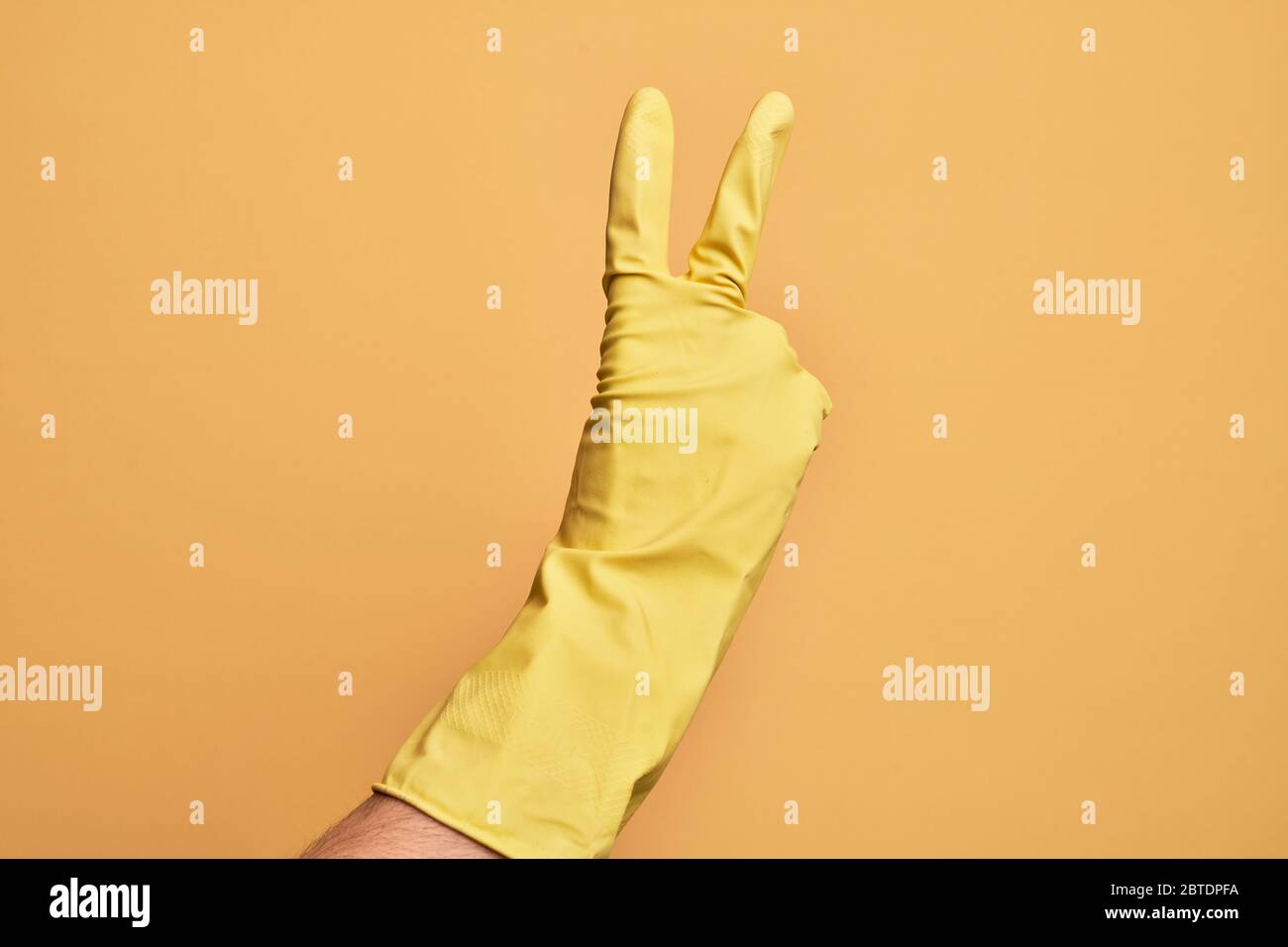 Hand of caucasian young man with cleaning glove over isolated yellow ...