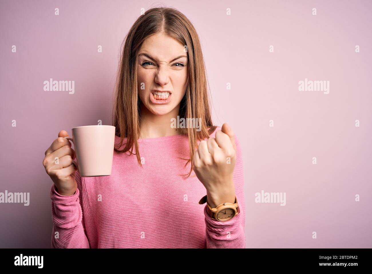 Young beautiful redhead woman drinking mug of coffee over isolated pink ...