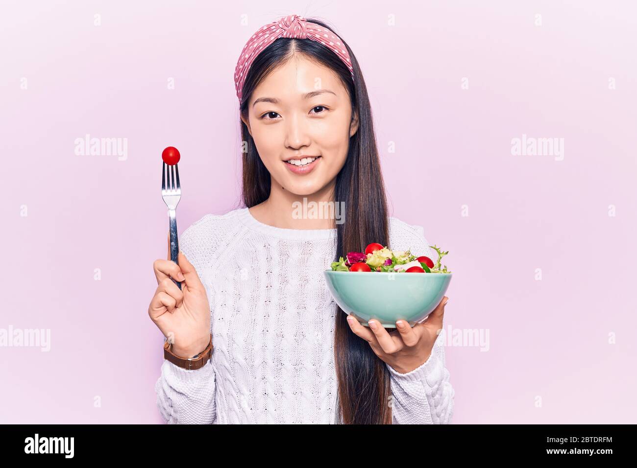 Young beautiful chinese woman eating bowl with salad looking positive ...