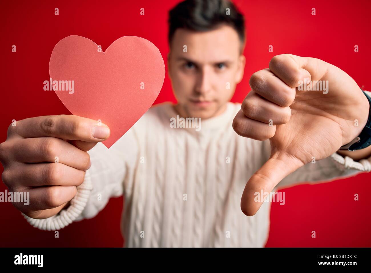 Young handsome caucasian man holding paper shape heart over red ...