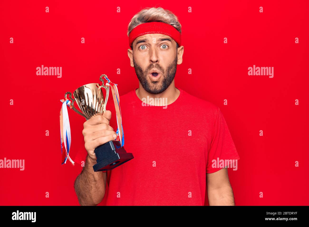 Young handsome blond sportsman with beard winning trophy over isolated ...
