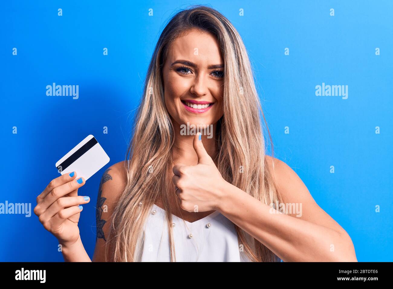 Young beautiful blonde woman holding credit card over isolated blue ...