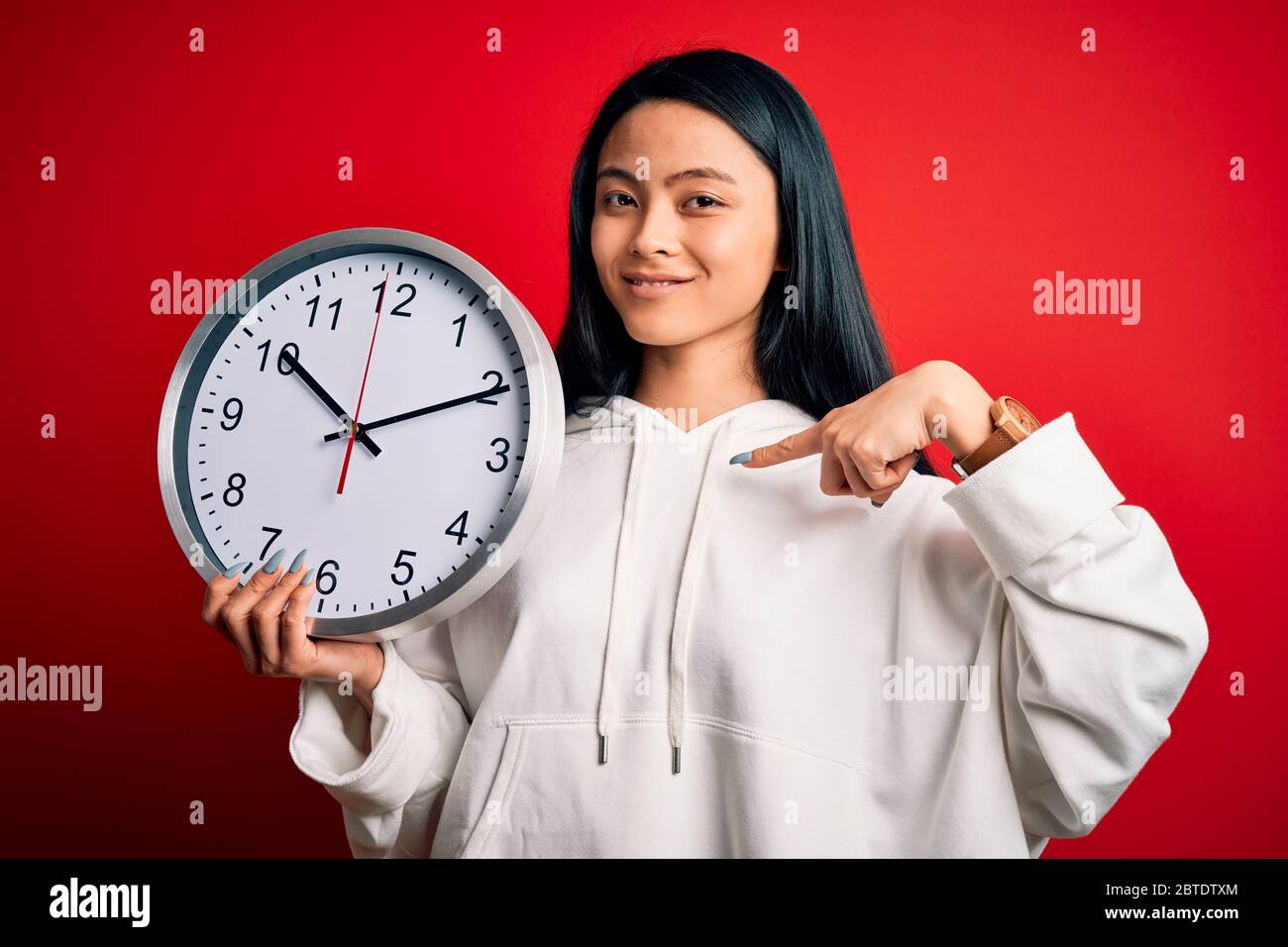 Young beautiful chinese woman holding big clock standing over isolated ...