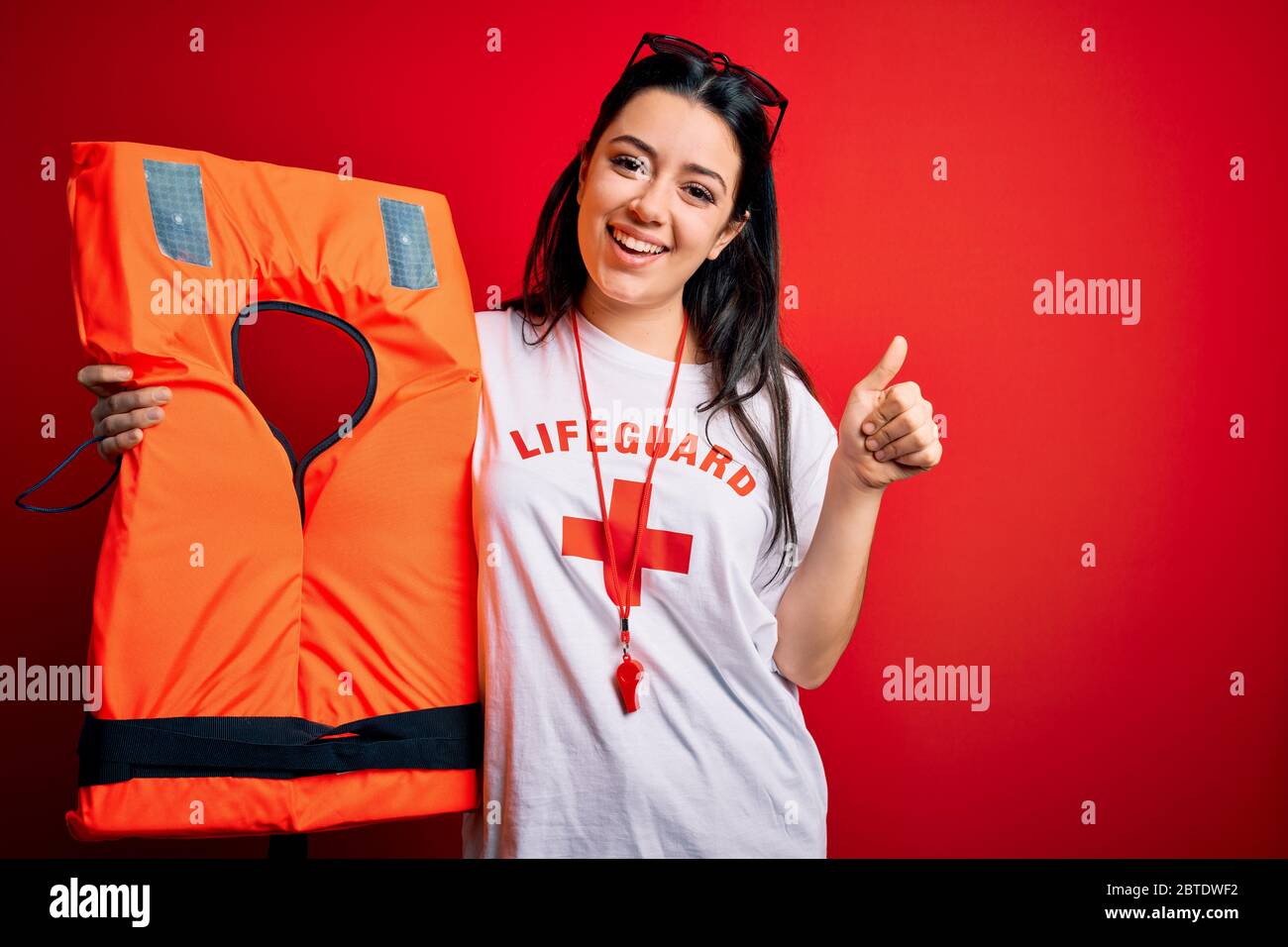Young lifeguard woman holding rescue lifejacket over red background ...
