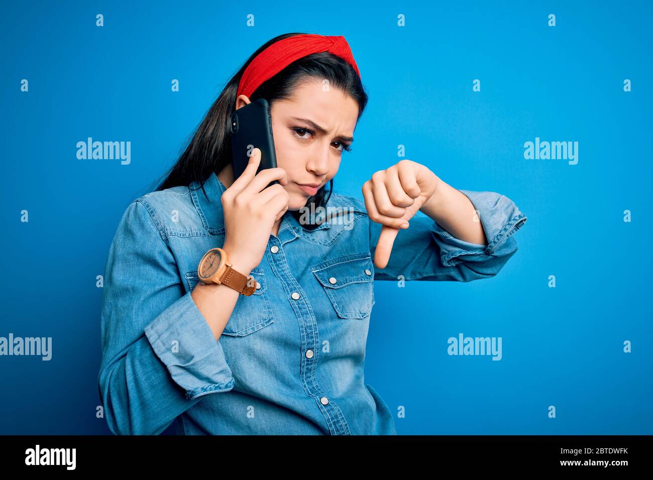 Young brunette woman talking on smartphone over blue isolated ...