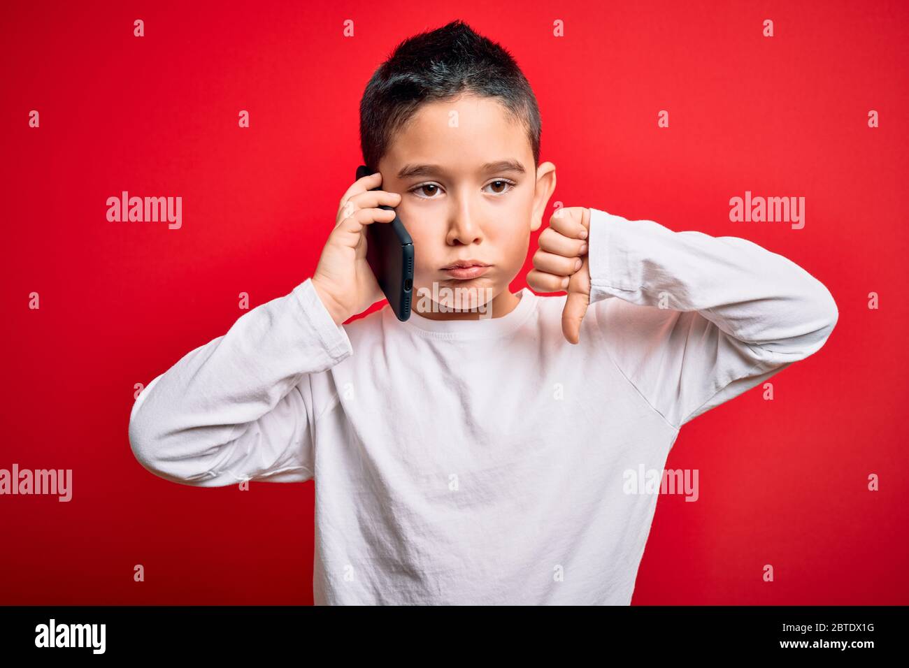 Young little boy kid talking on smartphone mobile over red isolated ...